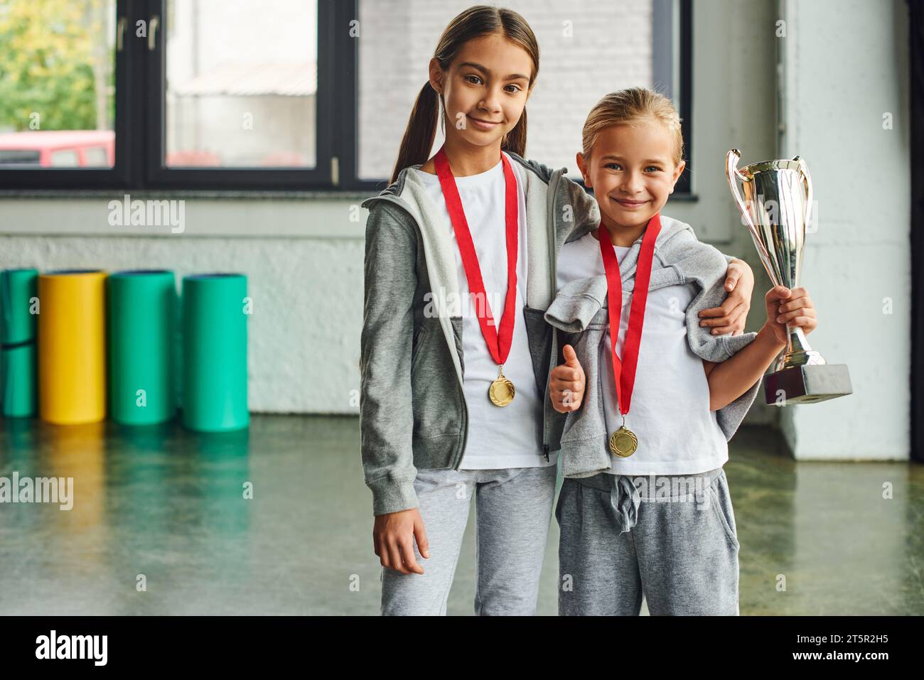 two cute preadolescent girls with medals holding trophy, smiling at ...