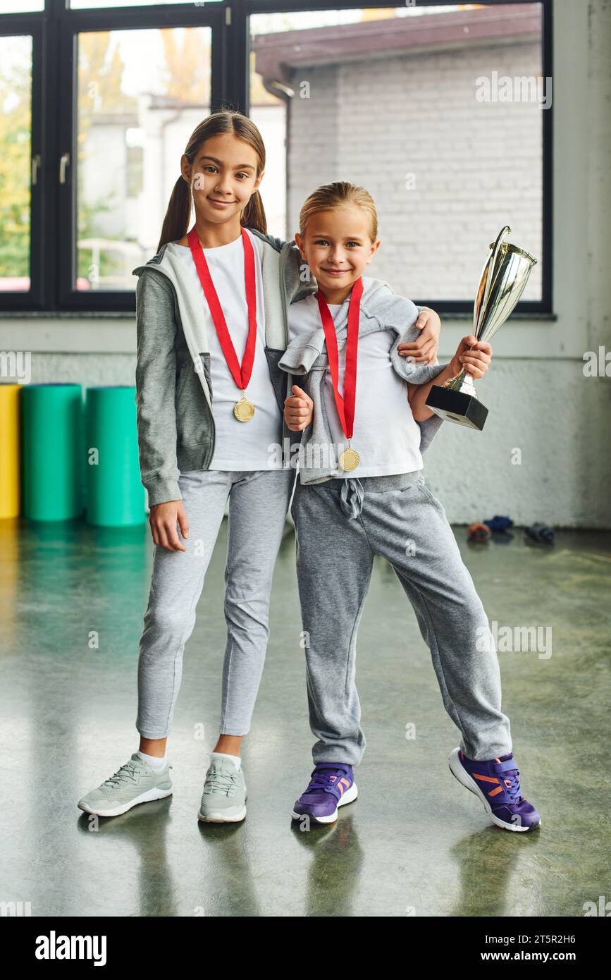 vertical shot of cute preadolescent girls with medals and trophy ...