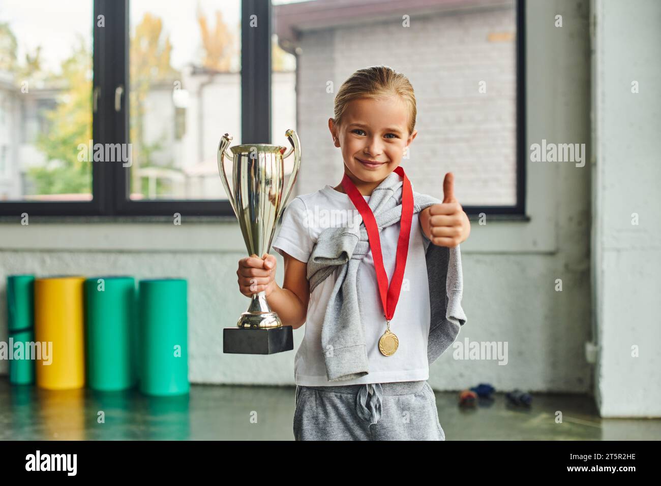cheerful preadolescent girl with golden medal showing thumb up and ...