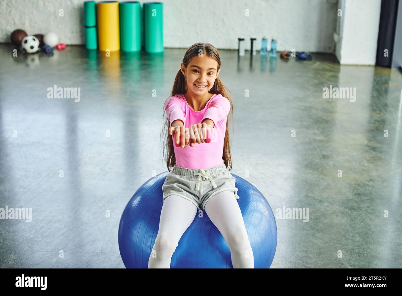 preadolescent cute girl in pink sportswear exercising with dumbbell on ...