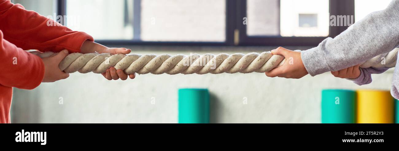 cropped view of two children in sportswear pulling fitness rope in gym ...