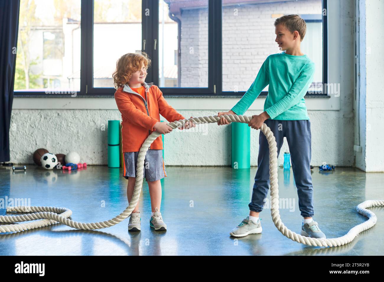 red haired and brunette boys in sportswear pulling fitness rope and ...