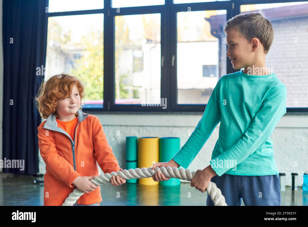 two preadolescent boys in sportswear pulling fitness rope and smiling ...