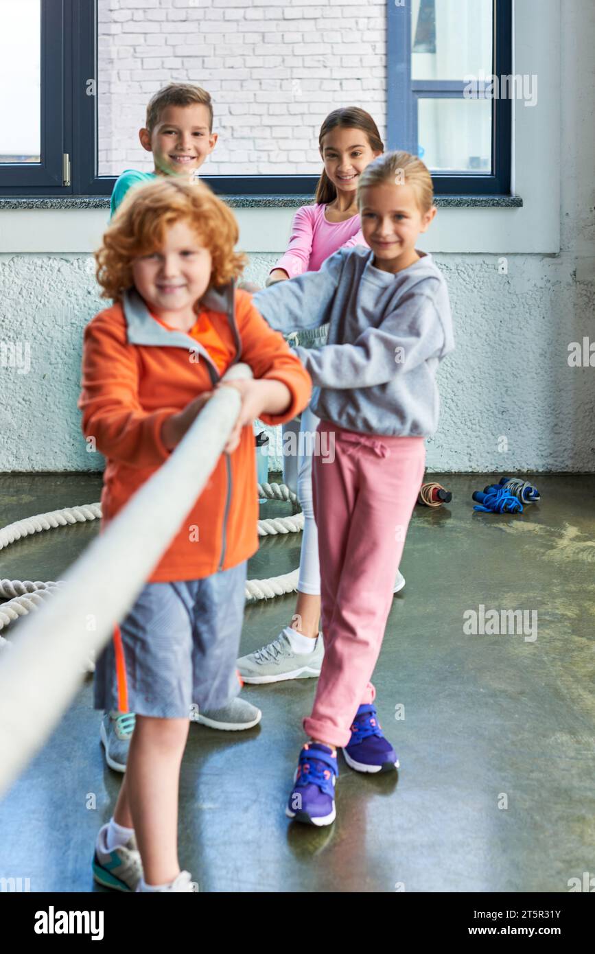 vertical shot of four jolly preadolescent boys and girls playing tug of ...