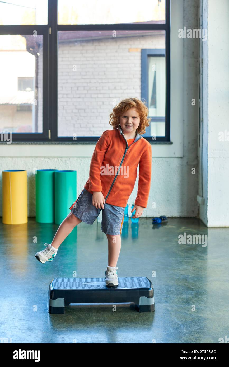 vertical shot of red haired jolly boy standing on one leg on fitness ...