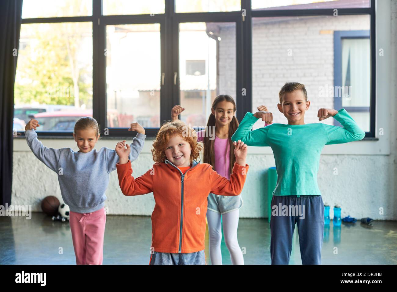 four pretty little children in sportswear playing muscles and smiling ...