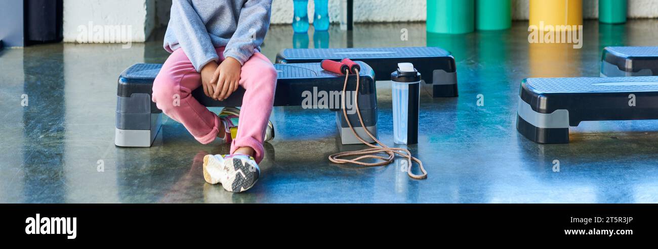 cropped view of little girl sitting on fitness stepper with water ...