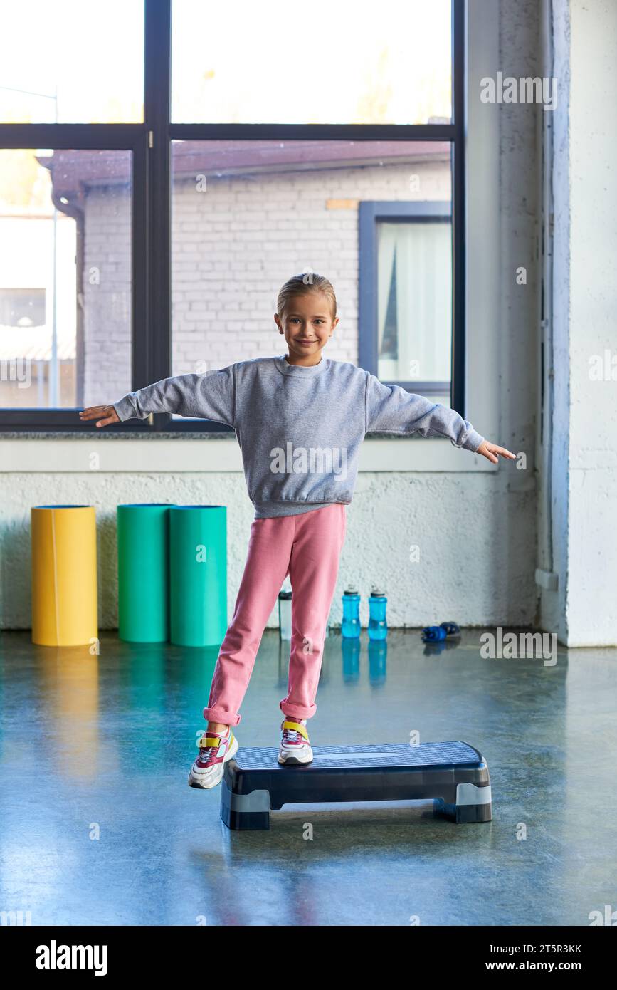 vertical shot of little cute girl stretching on fitness stepper and ...