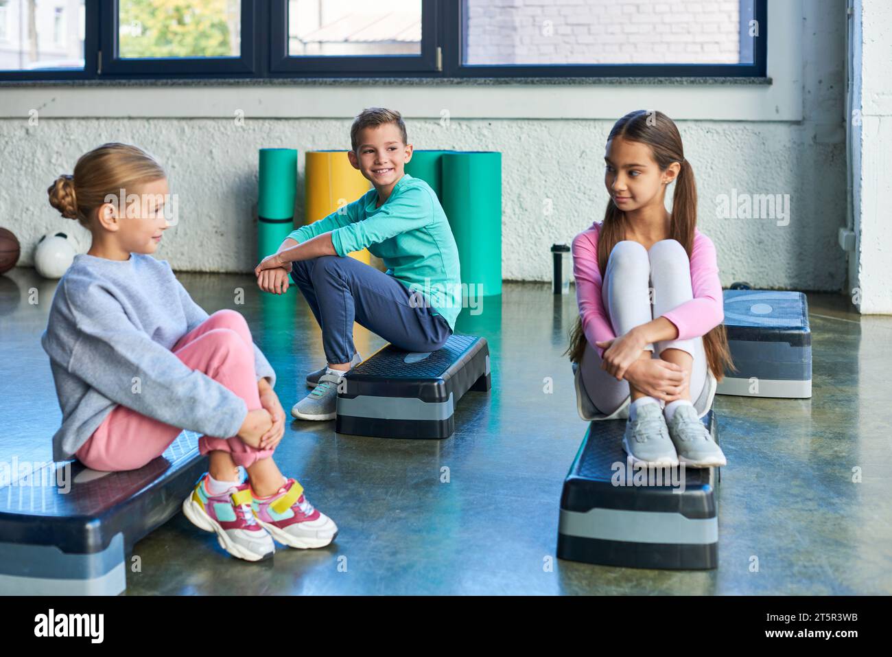 two pretty girls and boy sitting on fitness steppers and smiling at ...