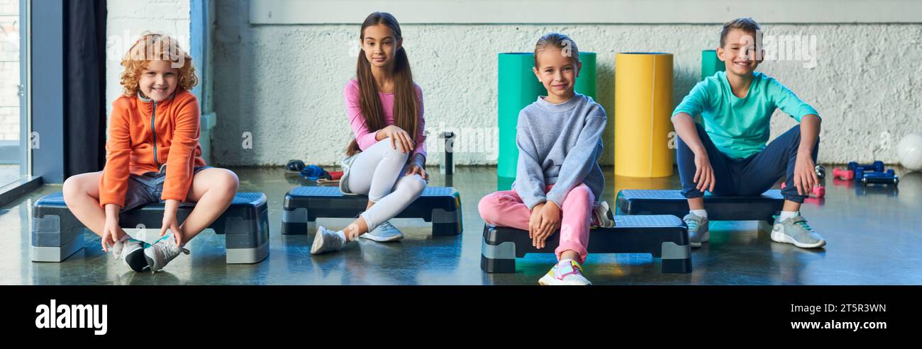 four cute little children sitting on fitness steppers and smiling at ...