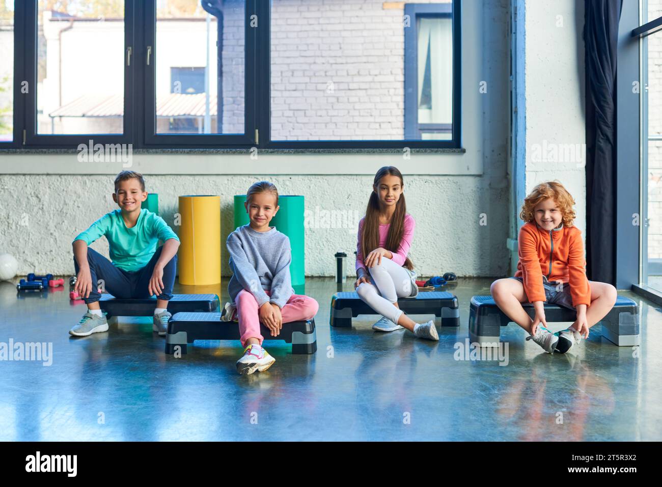 four preadolescent boys and girls sitting on fitness steppers and ...