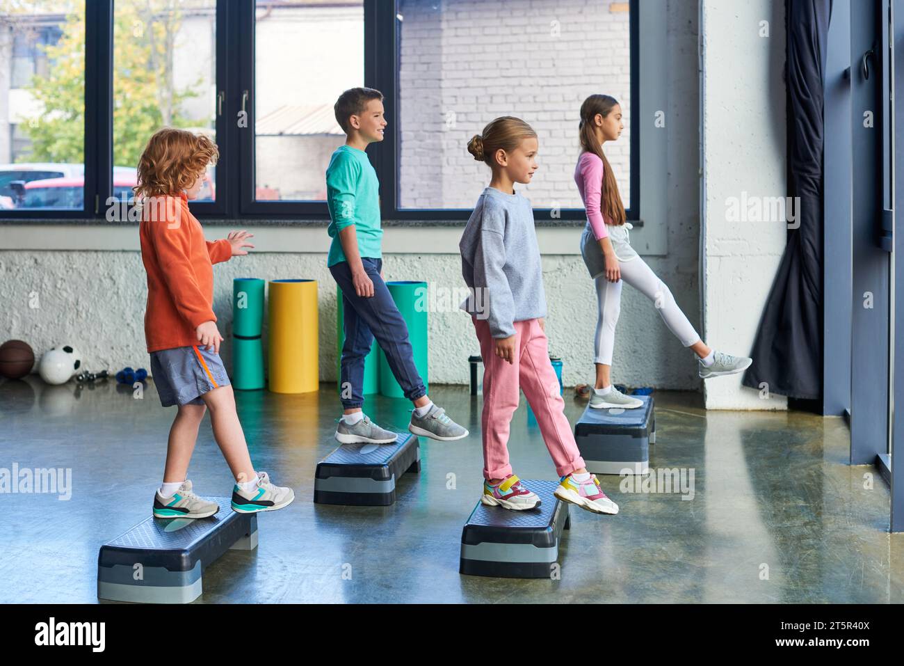 cute boys and girls in sportswear exercising on fitness stepper, raised ...