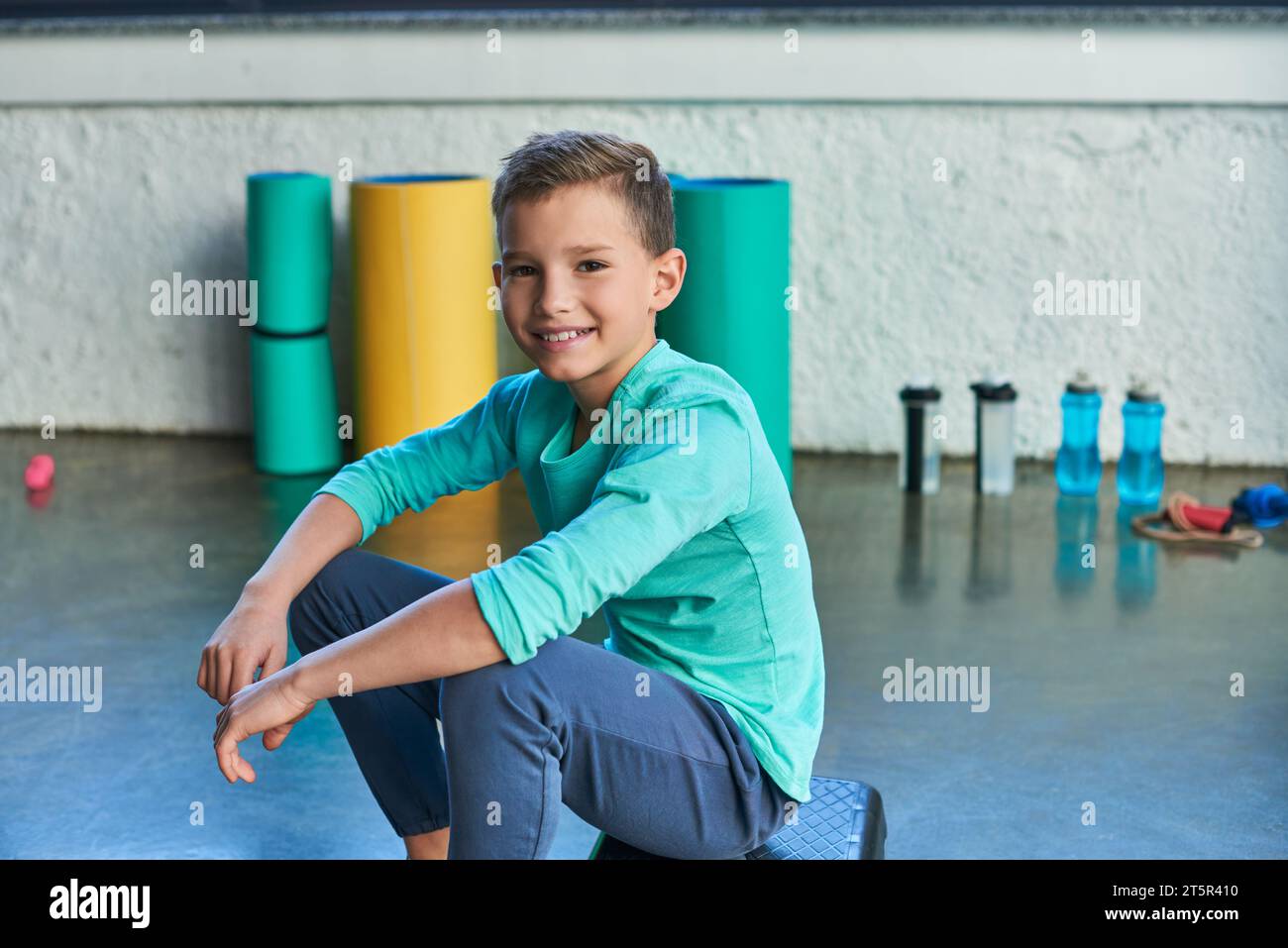 cheerful adolescent boy sitting on fitness stepper and smiling ...