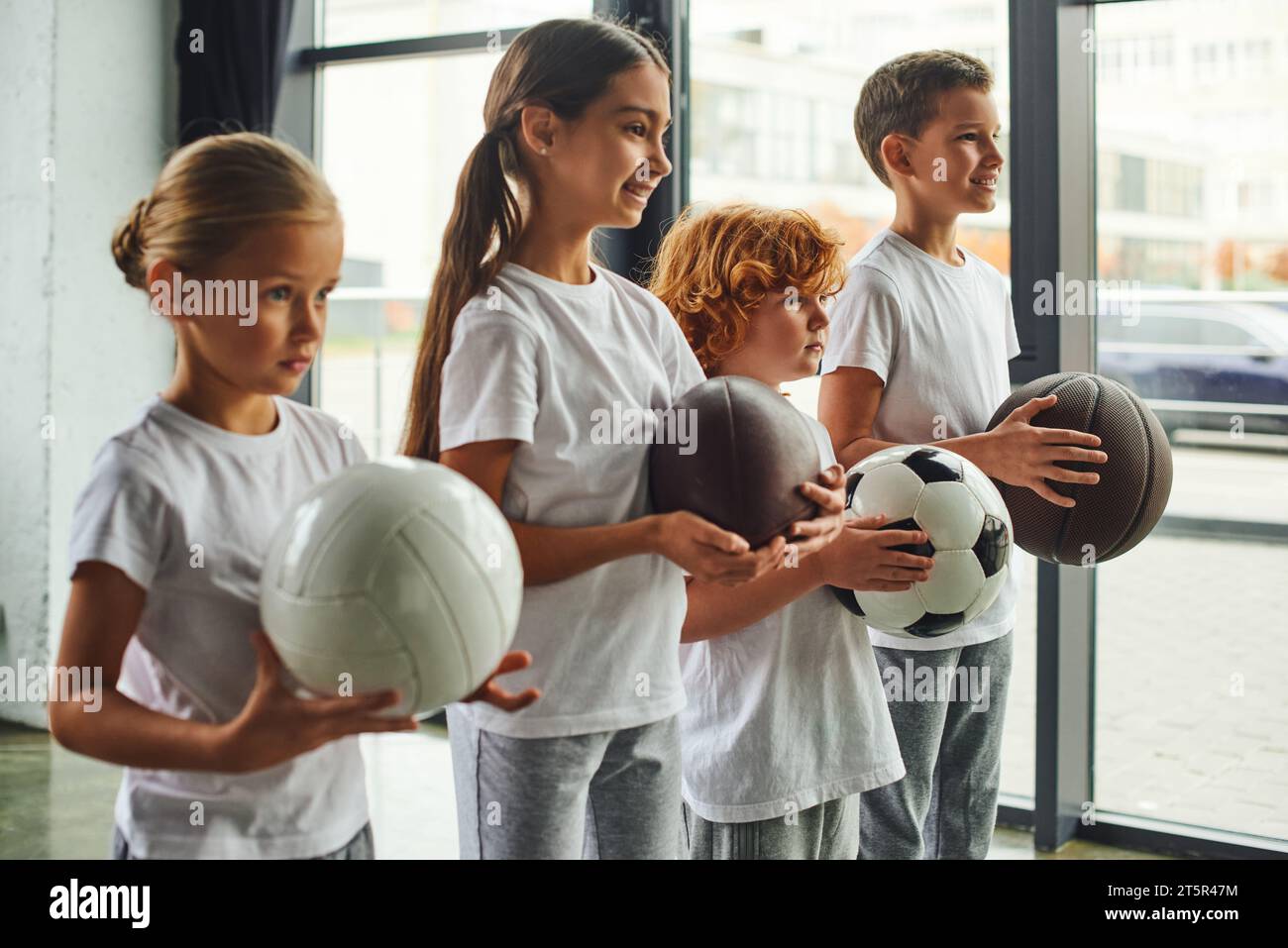 four cute preadolescent children with different kinds of balls posing ...