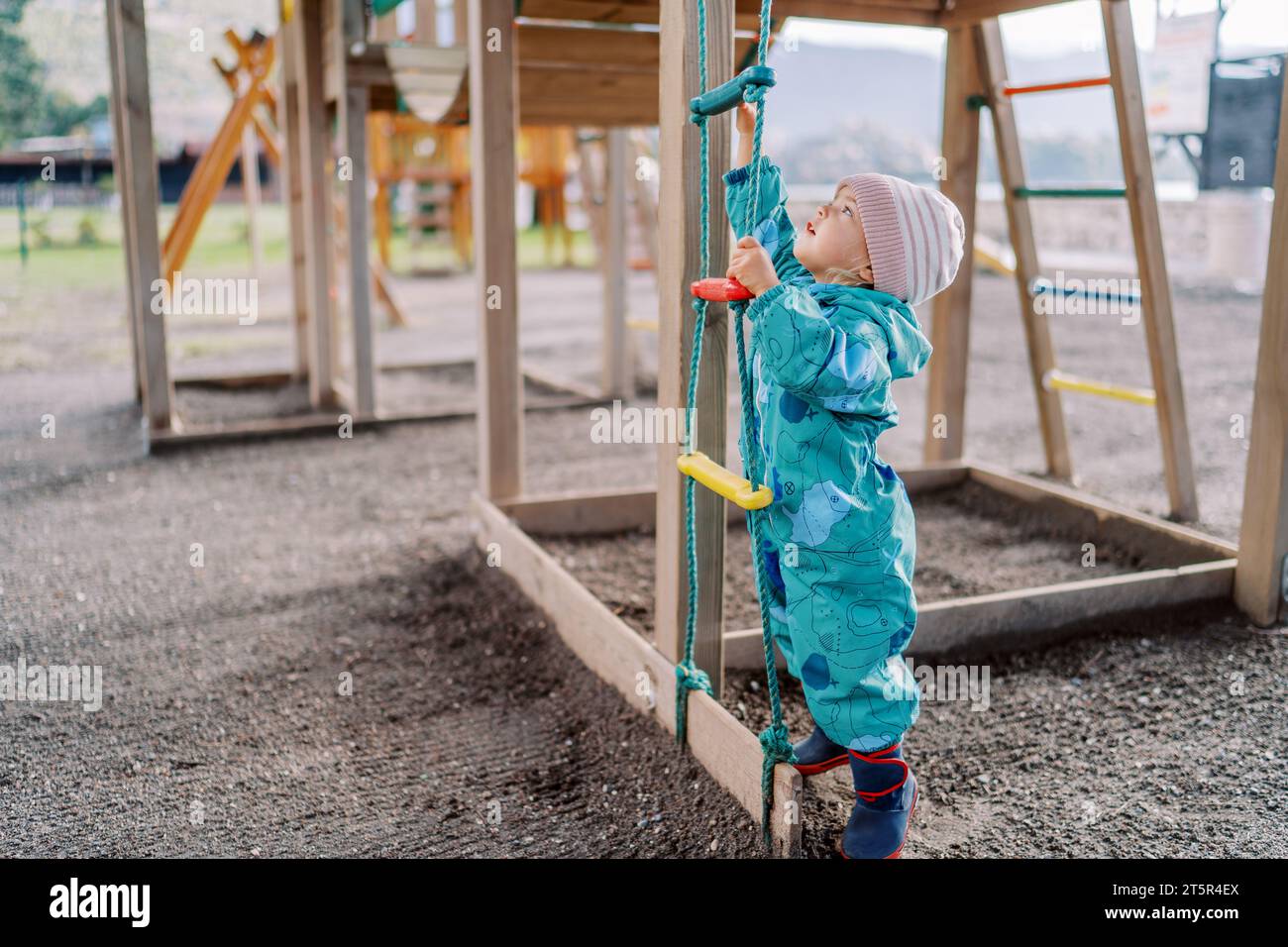 Little girl is trying to reach the top rung of a rope ladder by ...