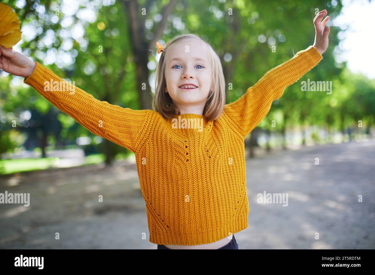 Adorable preschooler girl enjoying autumn day outdoors. Happy child gathering autumn leaves in ...
