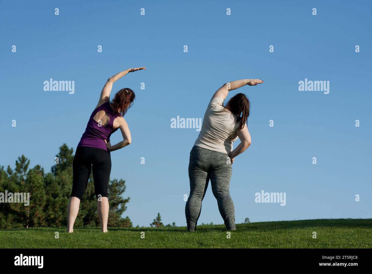 Two middle-aged women doing fitness in city park, bending body to side ...
