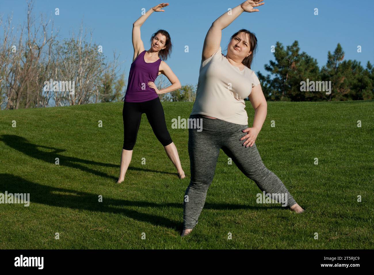 Two middle-aged women doing fitness in city park, bending body to side ...