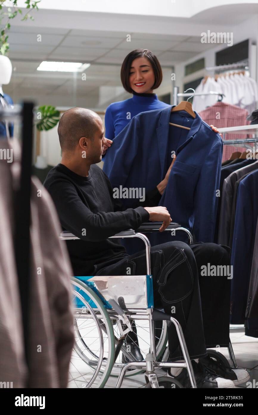 Boutique employee showing jacket on hanger while arab man in wheelchair ...