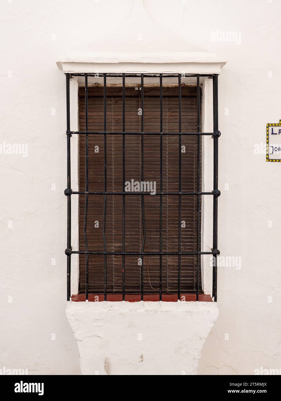 A old style window made of dark wood covered with a grill/guard set in ...