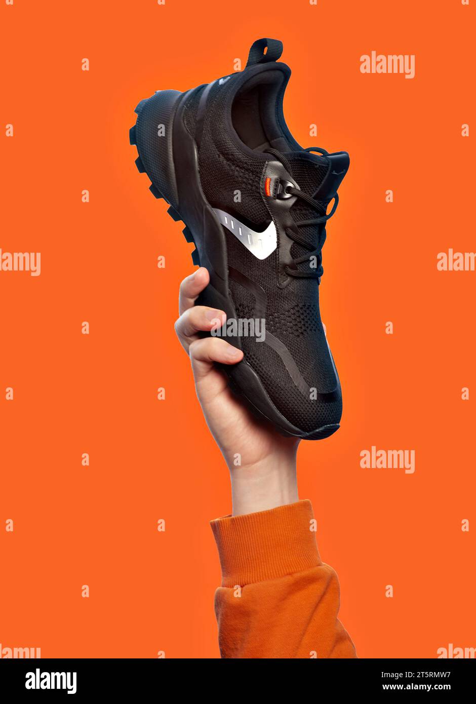 Modern black sneaker, held by a man's hand, isolated on a bright orange ...