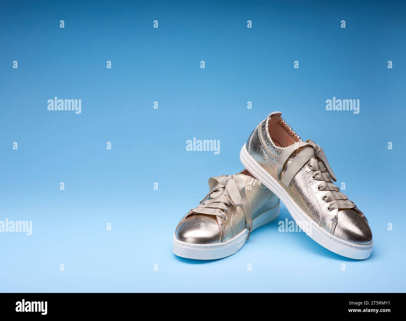 Modern sneakers in metallic gold leather on a gradient blue background ...