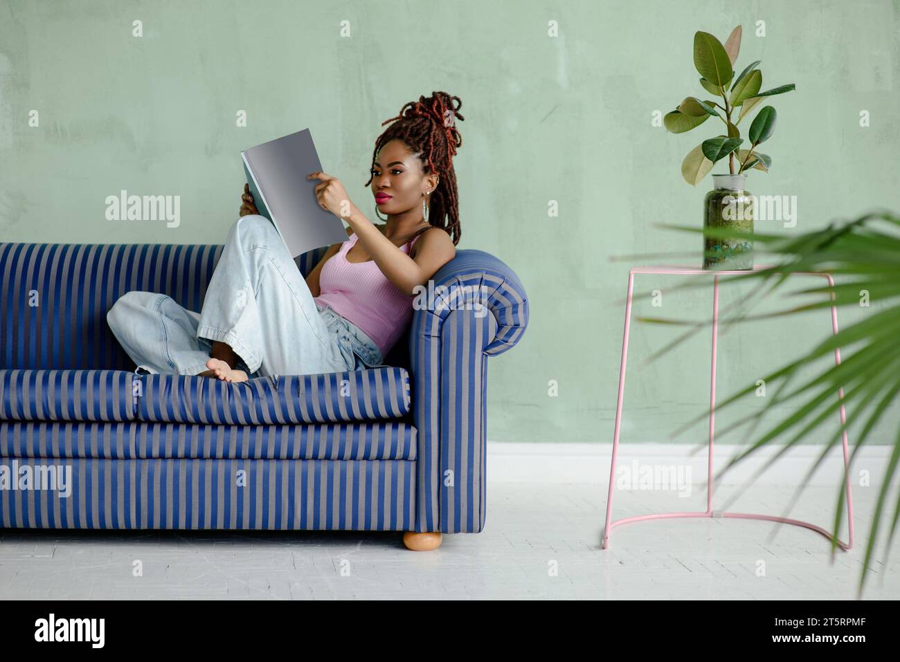 Pretty African young woman reading magazine and smiling while sitting ...