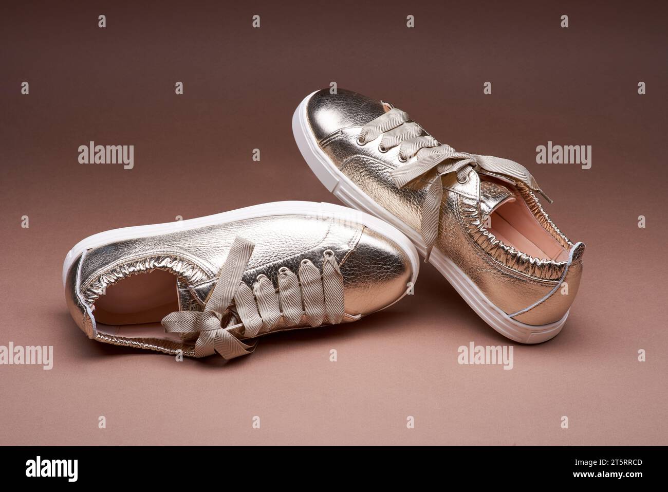 New golden metallic sneakers with white rubber soles on a gradient ...