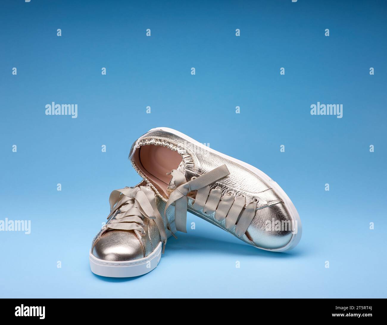 A pair of shiny golden metallic sneakers on a gradient blue background ...