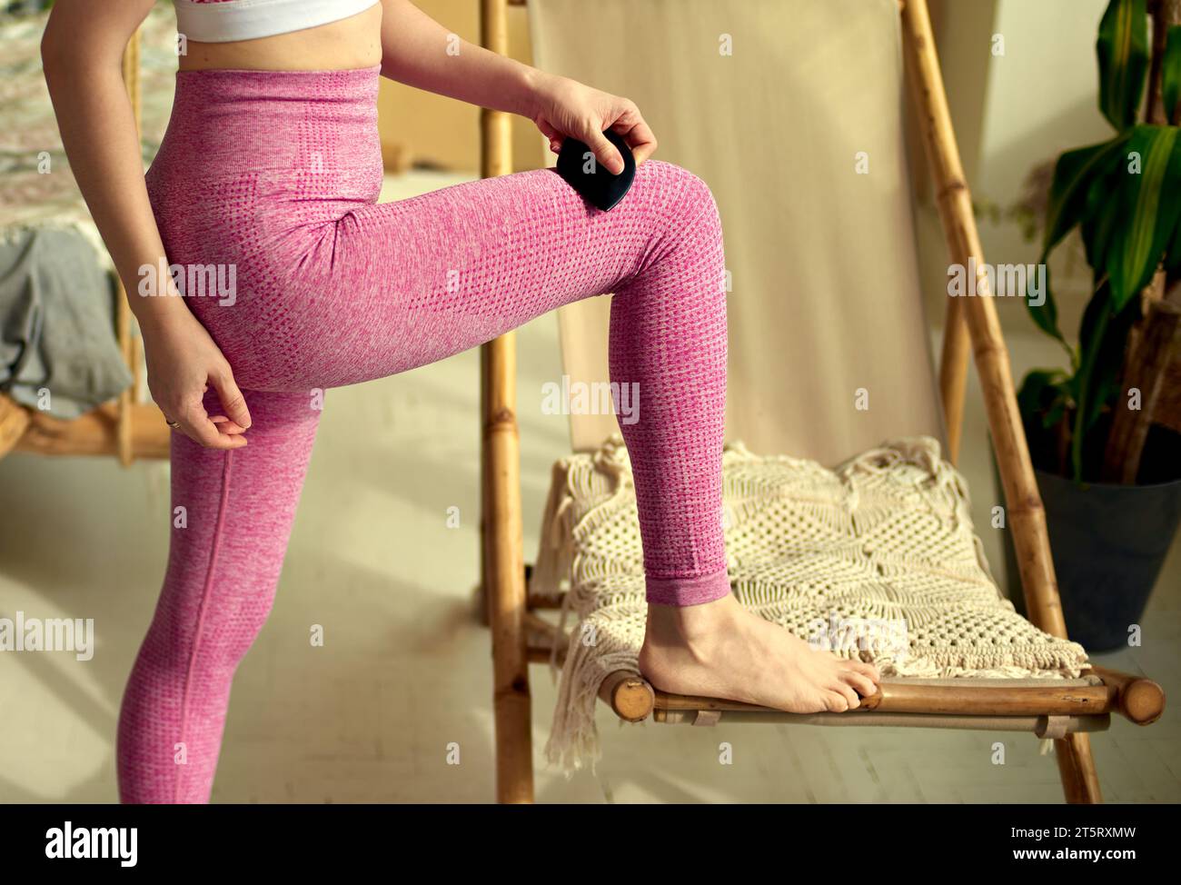 Woman wears pink leggings applying gua sha black comb edge to her leg ...
