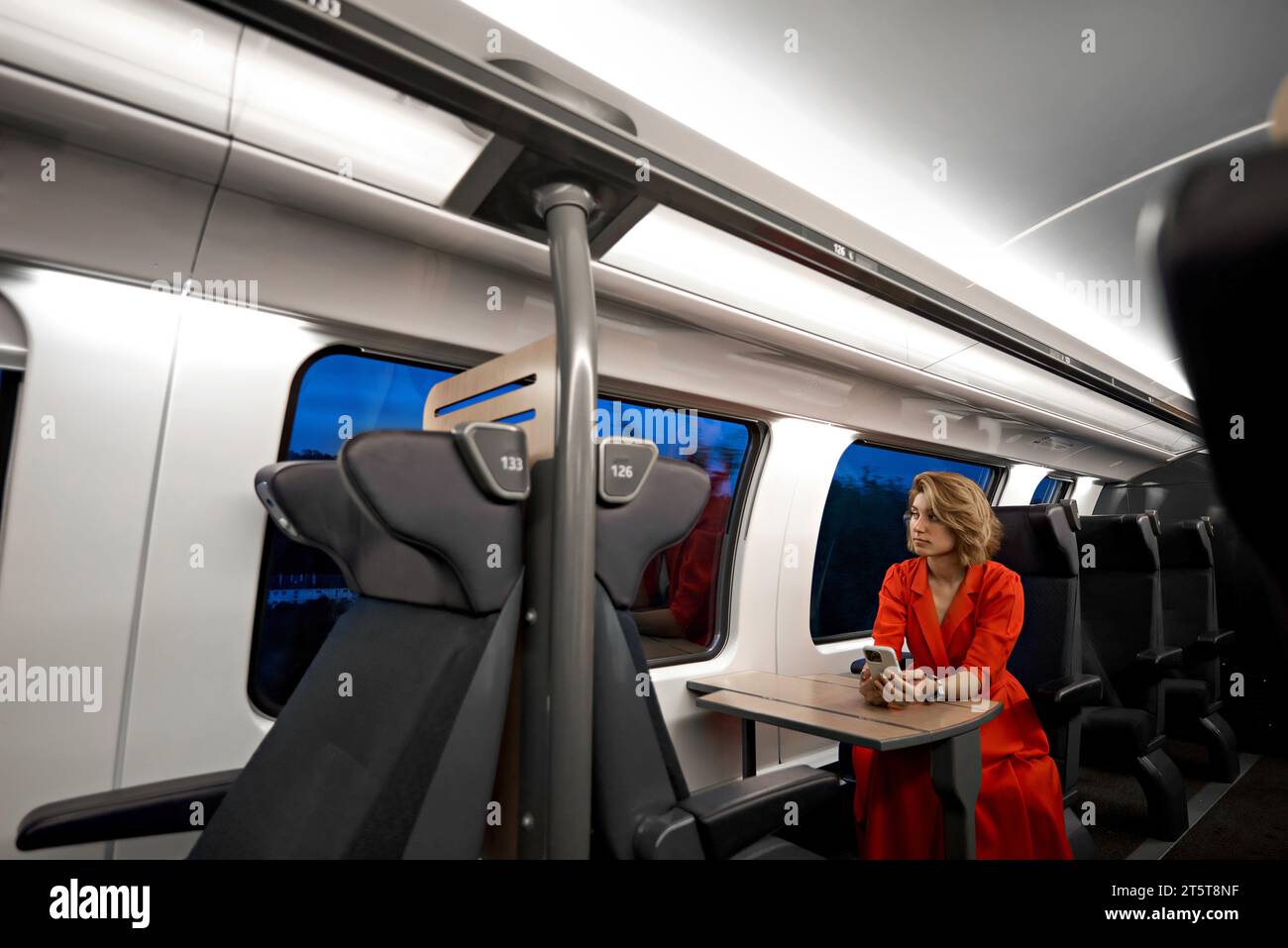 Young Caucasian female in red dress looking out window while riding ...