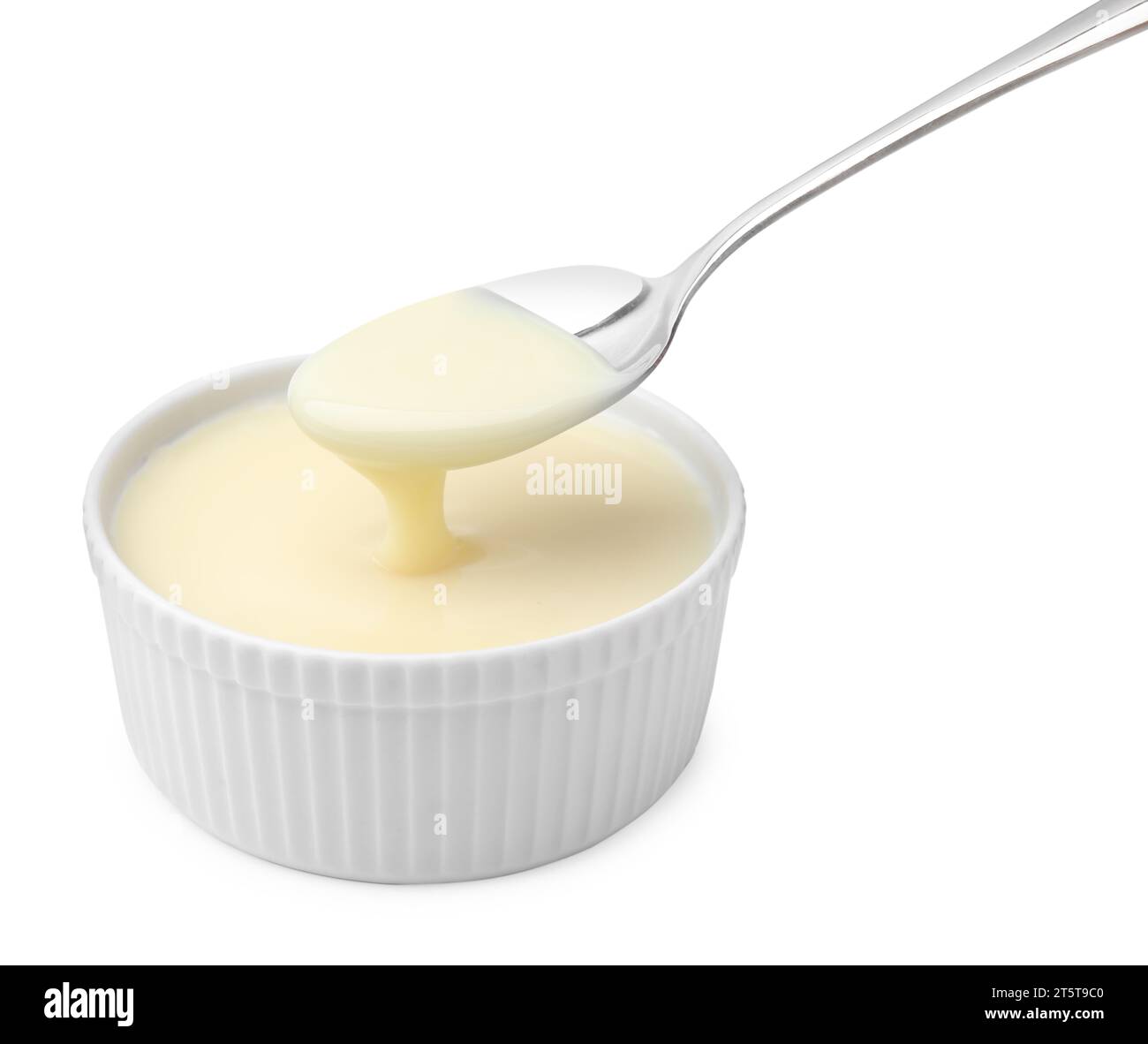 Condensed milk flowing down from spoon into bowl isolated on white ...