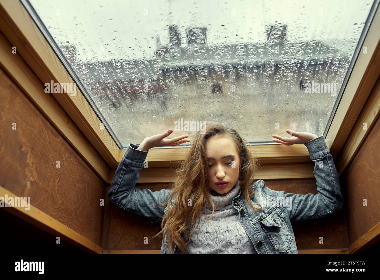 Girl with closed eyes touches the window in the ceiling of the house ...