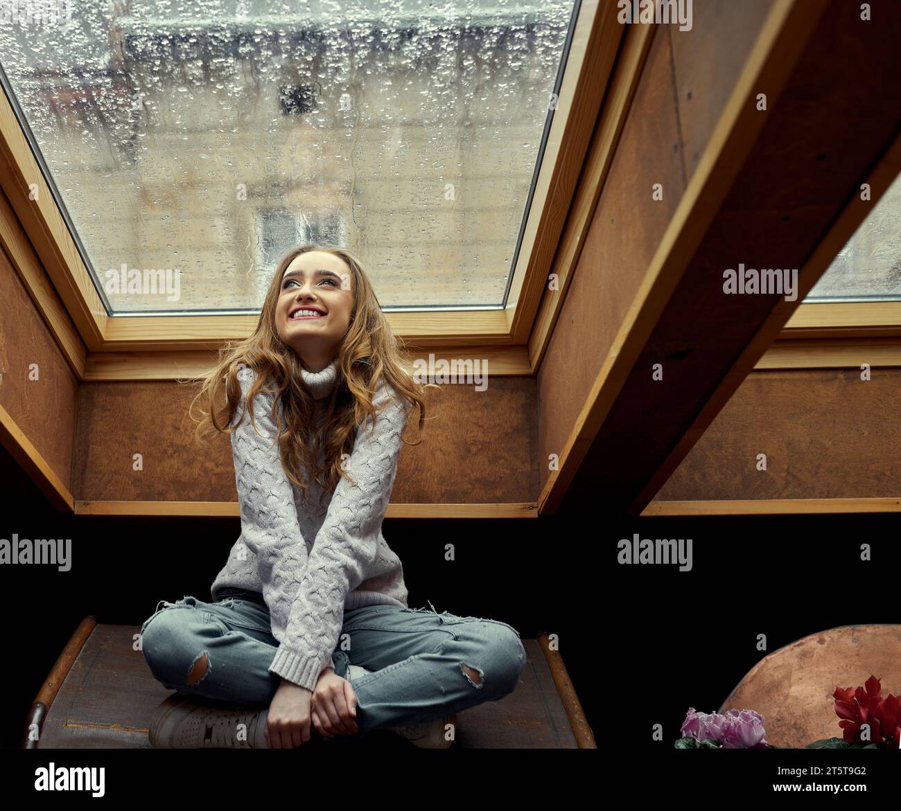 Young girl is happy about the rain outside the window, sitting in her ...