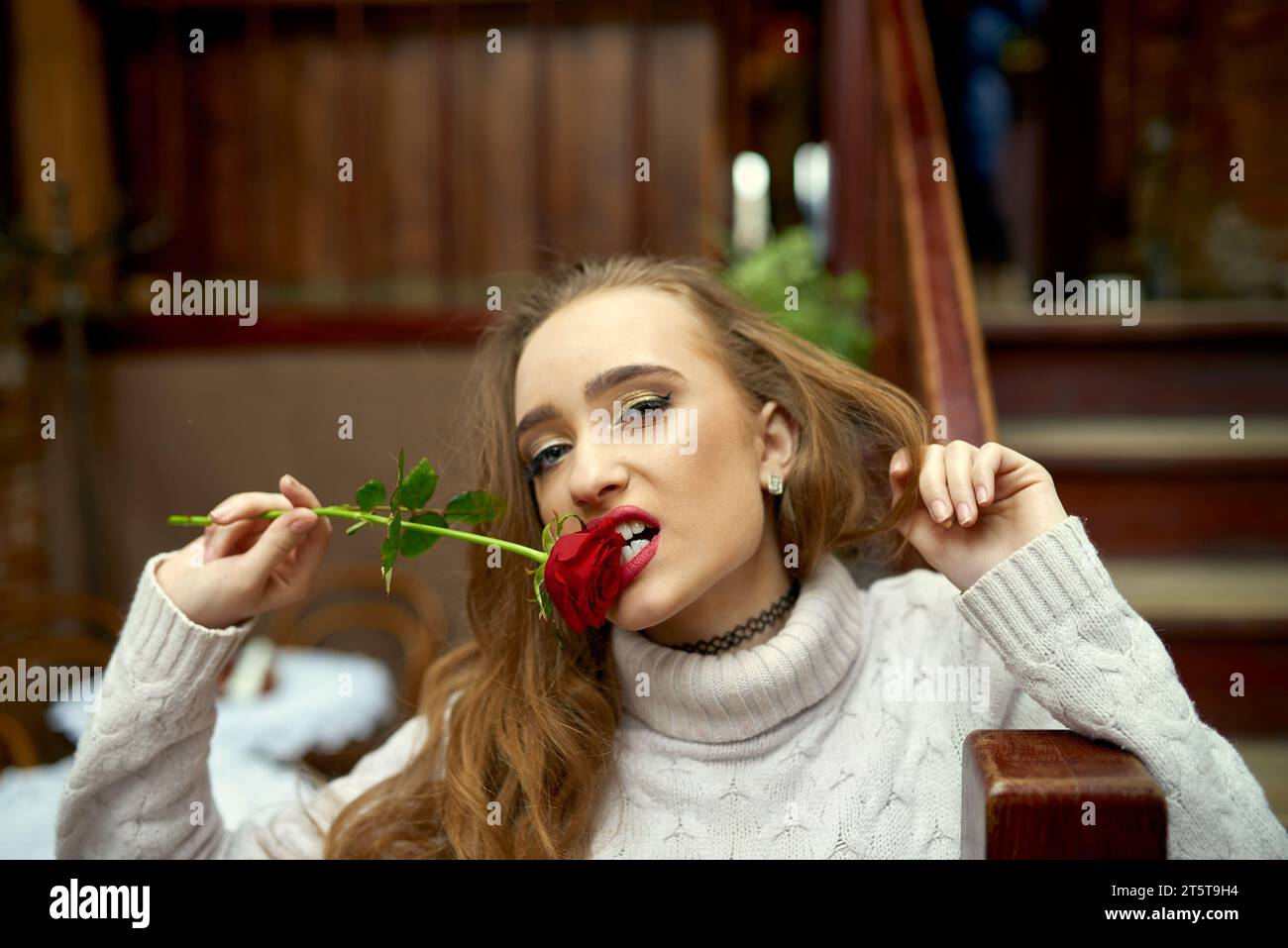 Young girl in a white sweater bites a gift rose trying to seduce her ...