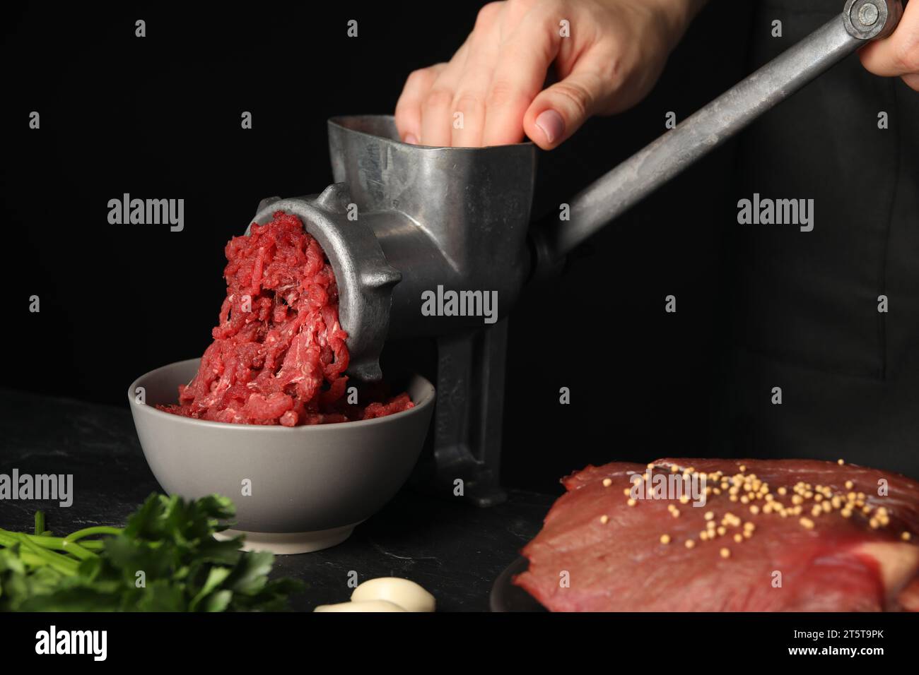 Woman making beef mince with manual meat grinder at table against black ...