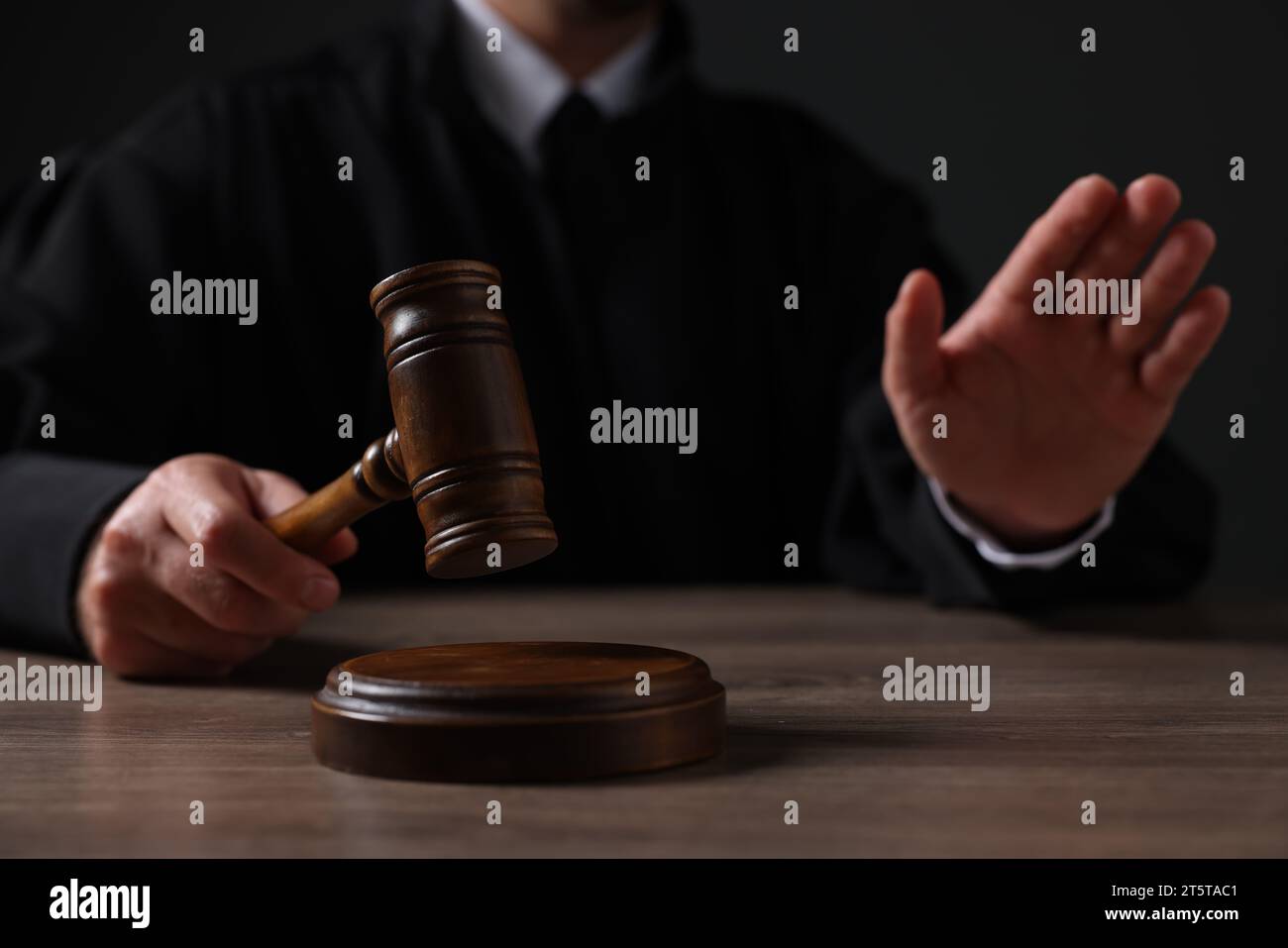 Judge with gavel showing stop gesture at wooden table against black ...