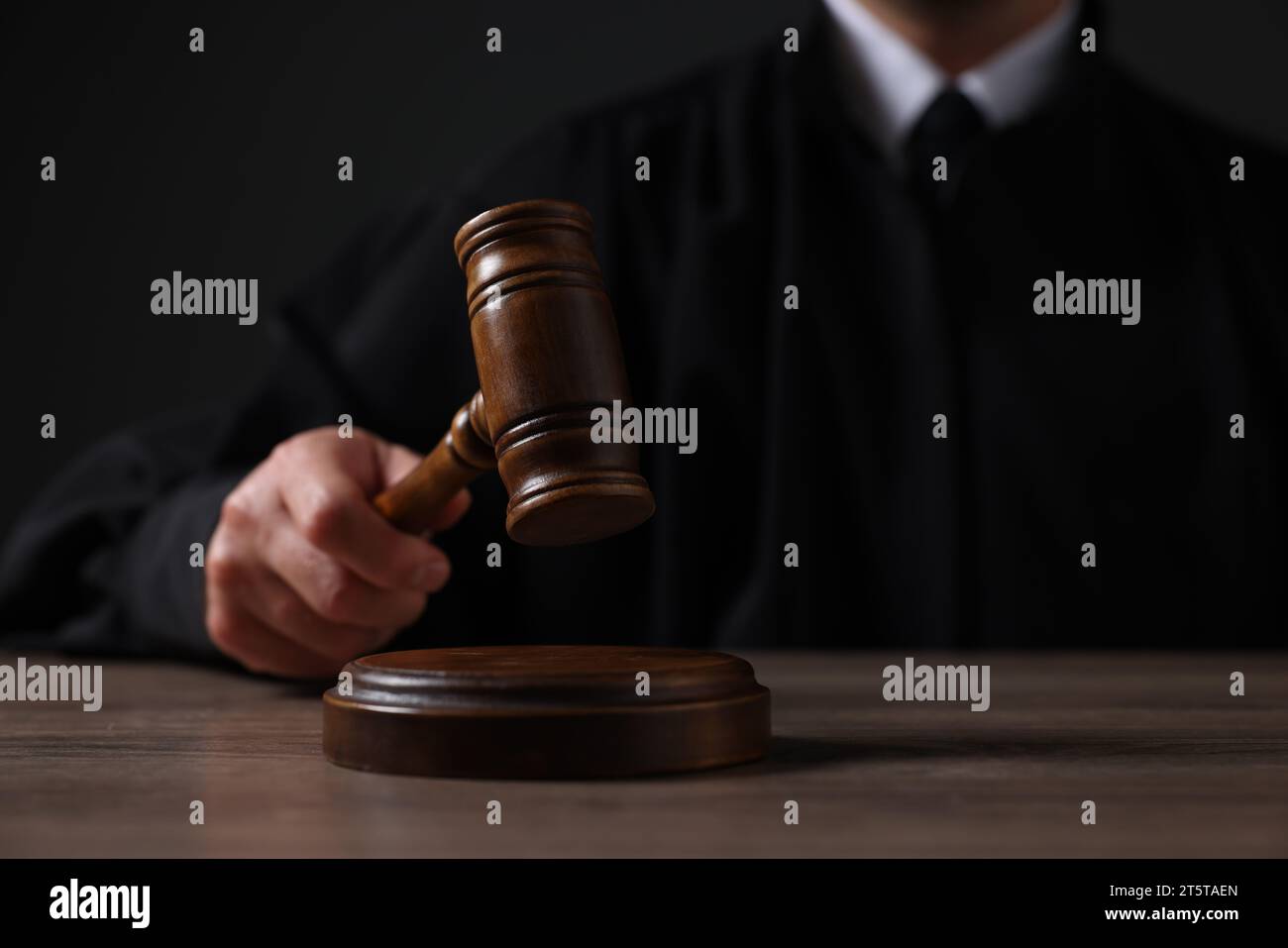 Judge with gavel sitting at wooden table against black background ...