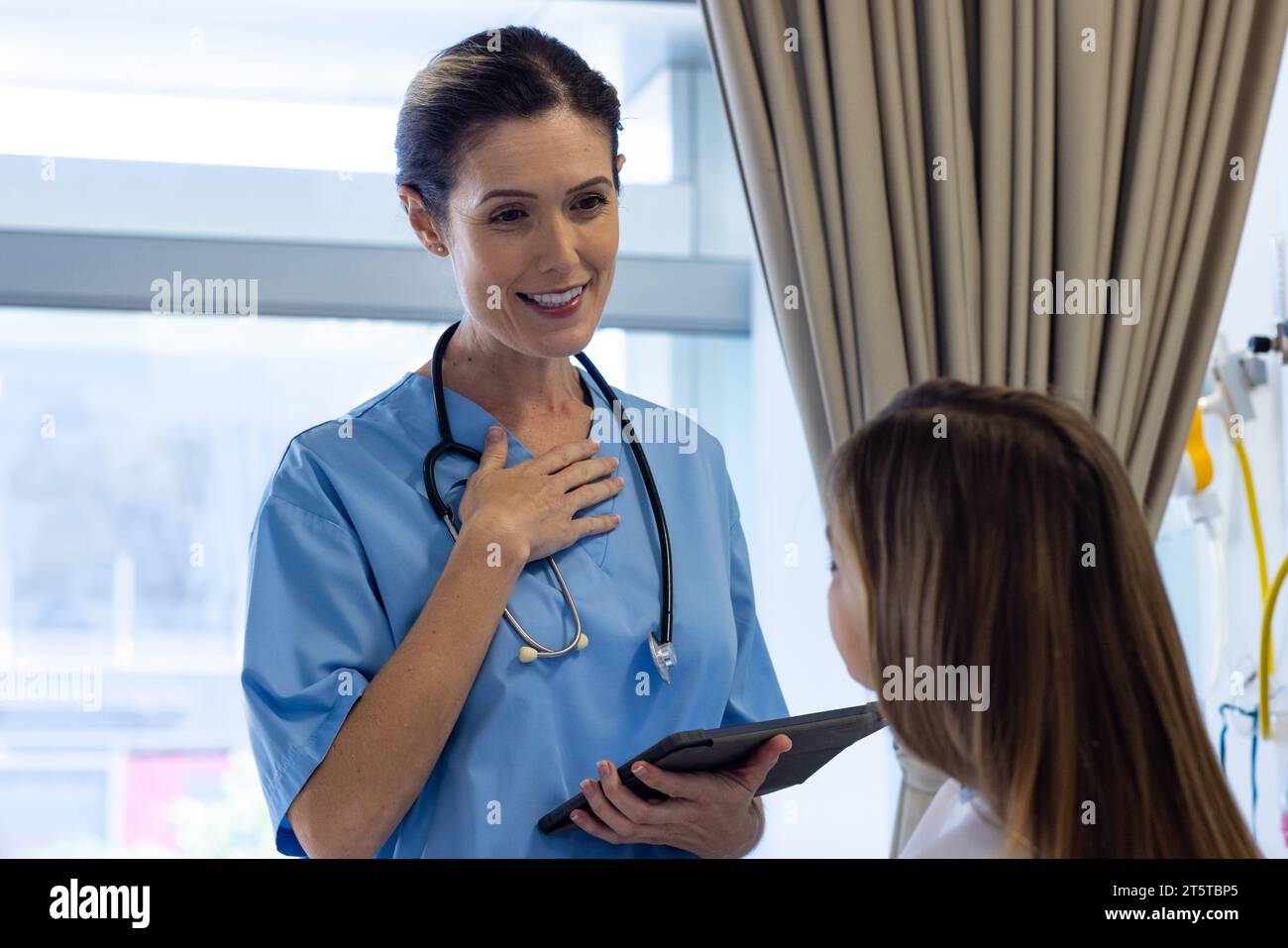 Smiling caucasian female doctor with tablet and girl patient talking in ...