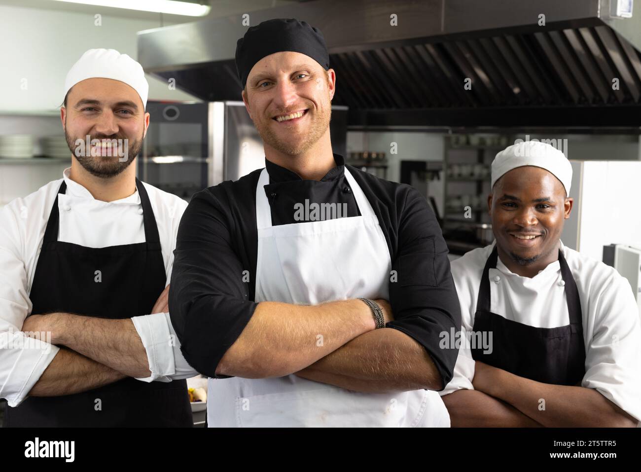 Three happy diverse male chefs standing with arms crossed in restaurant ...