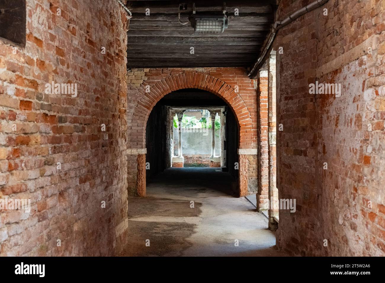 Old, empty arched hall or passage made of bricks with wooden beams in ...