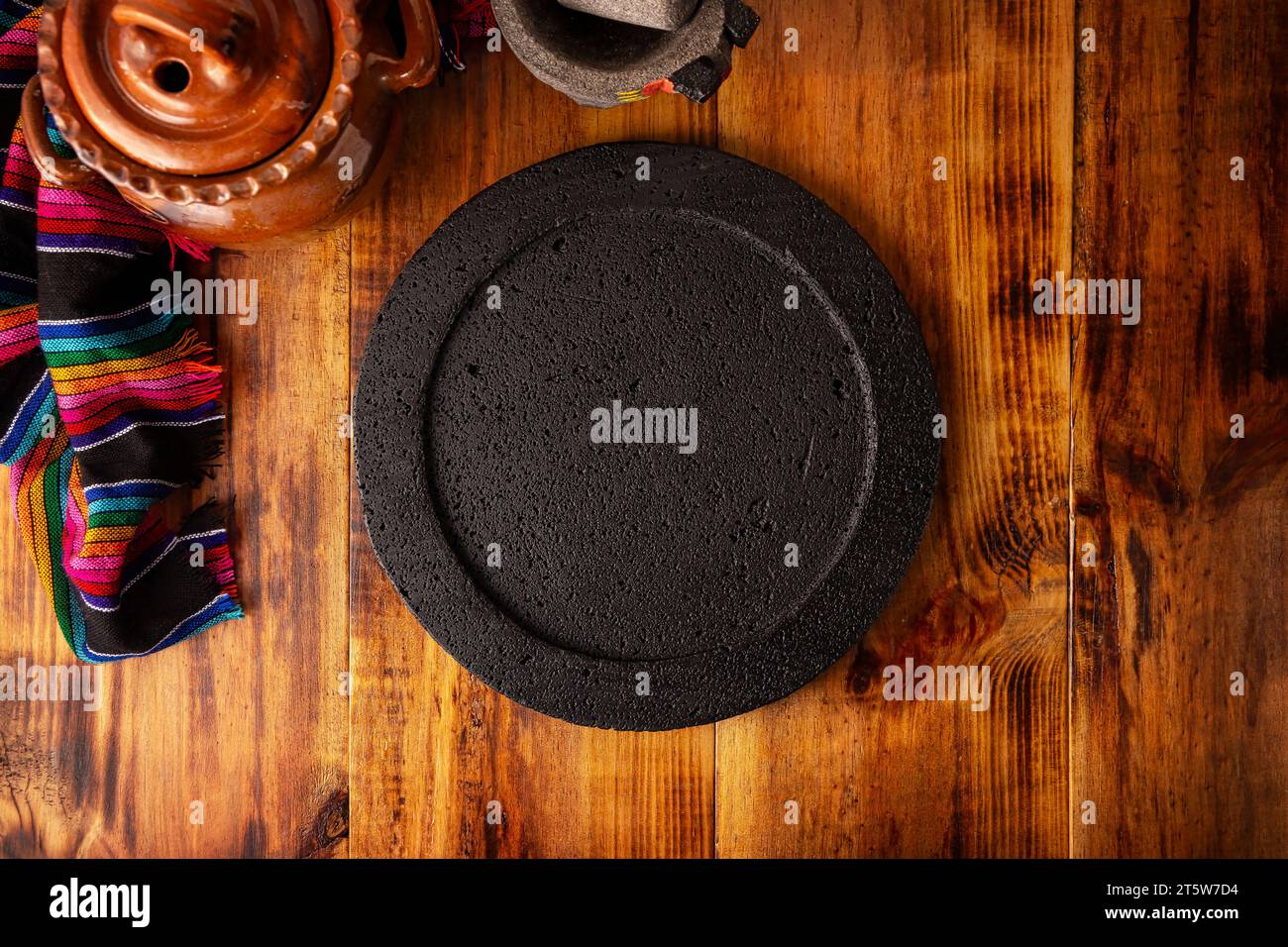 Empty stone comal plate on wooden rustic table, colorful typical ...