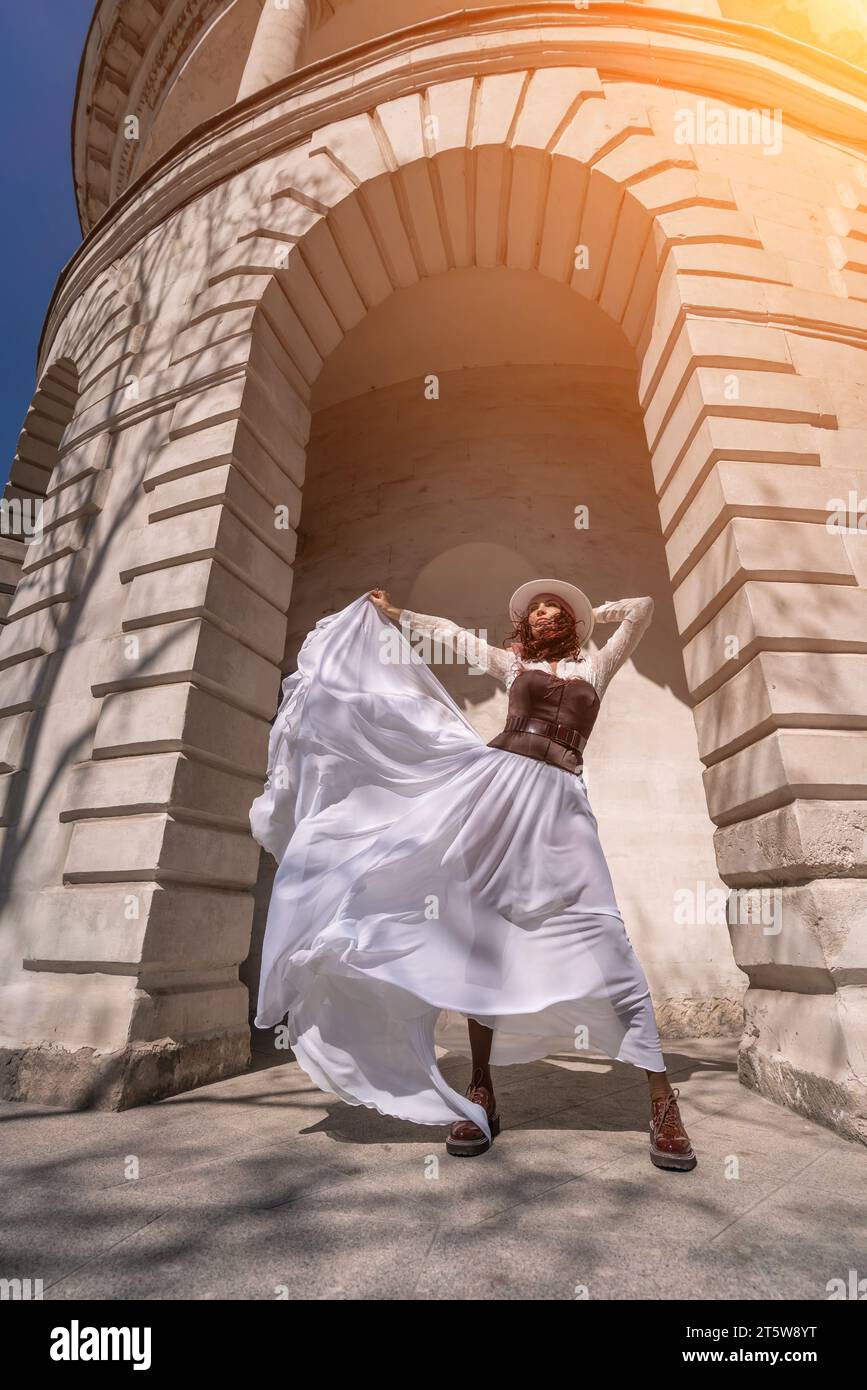 Stylish woman building city. A dancer in a long white skirt dances in ...