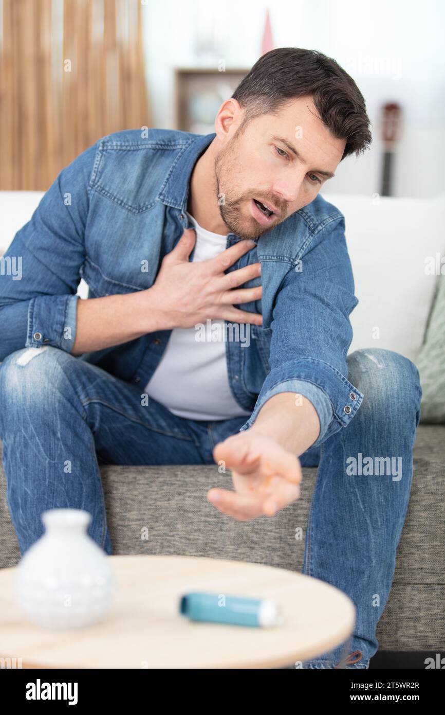 young man with asthma attack reaching for inhaler from table Stock ...