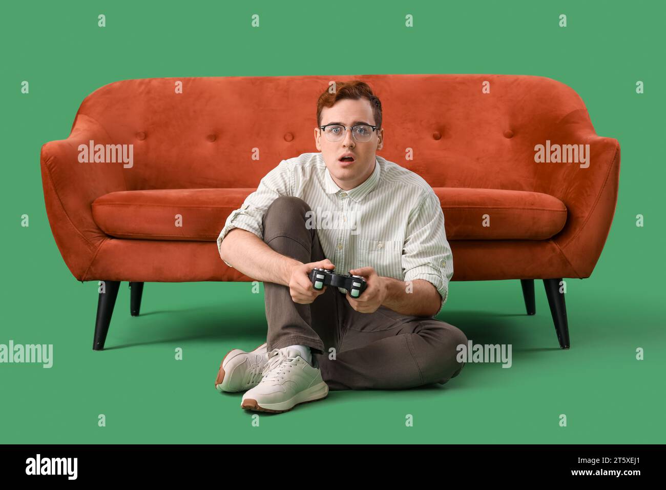 Shocked young man playing video game near red sofa on green background ...