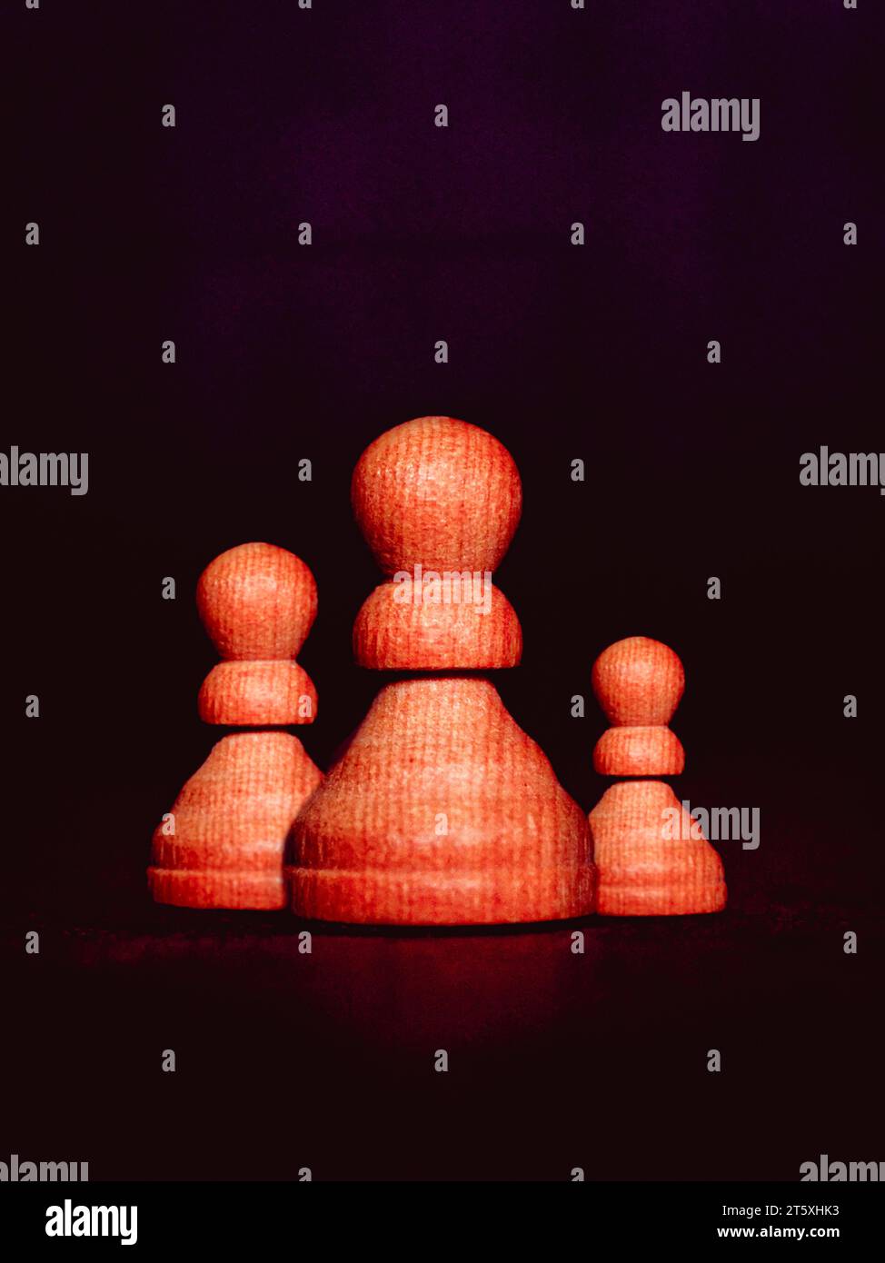 Three chess pieces, pawns, of different sizes against dark background ...
