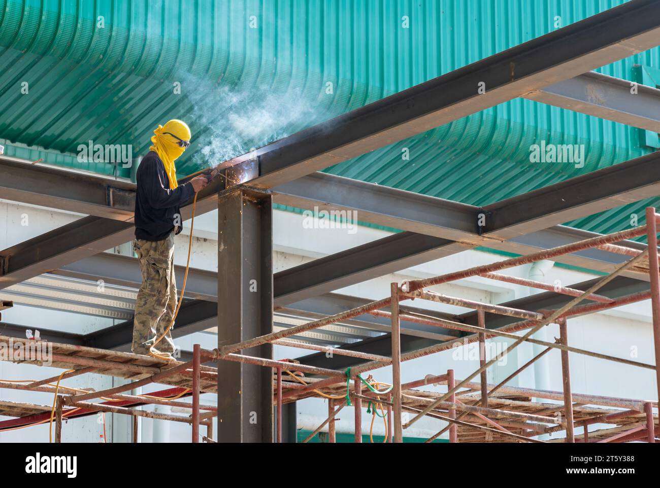 Worker Man welder stand on scaffolding support welds an iron beam in ...