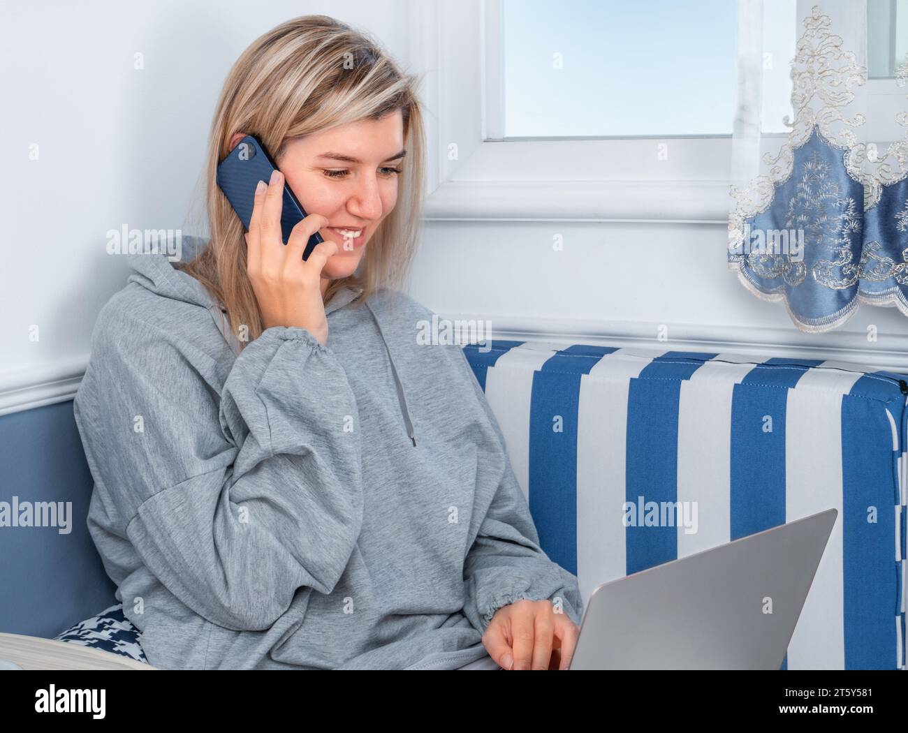 Girl talking on the phone with a smile and using a laptop near the ...
