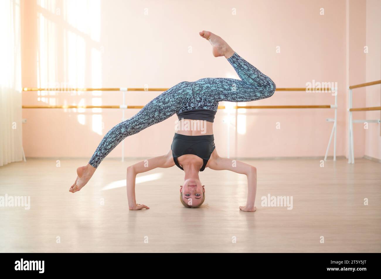 Flexible Caucasian girl stands on her head in a dance class. The girl ...