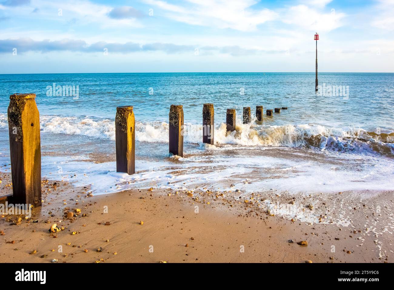 Looking out to sea with waves splashing onto classic wooden groynes ...